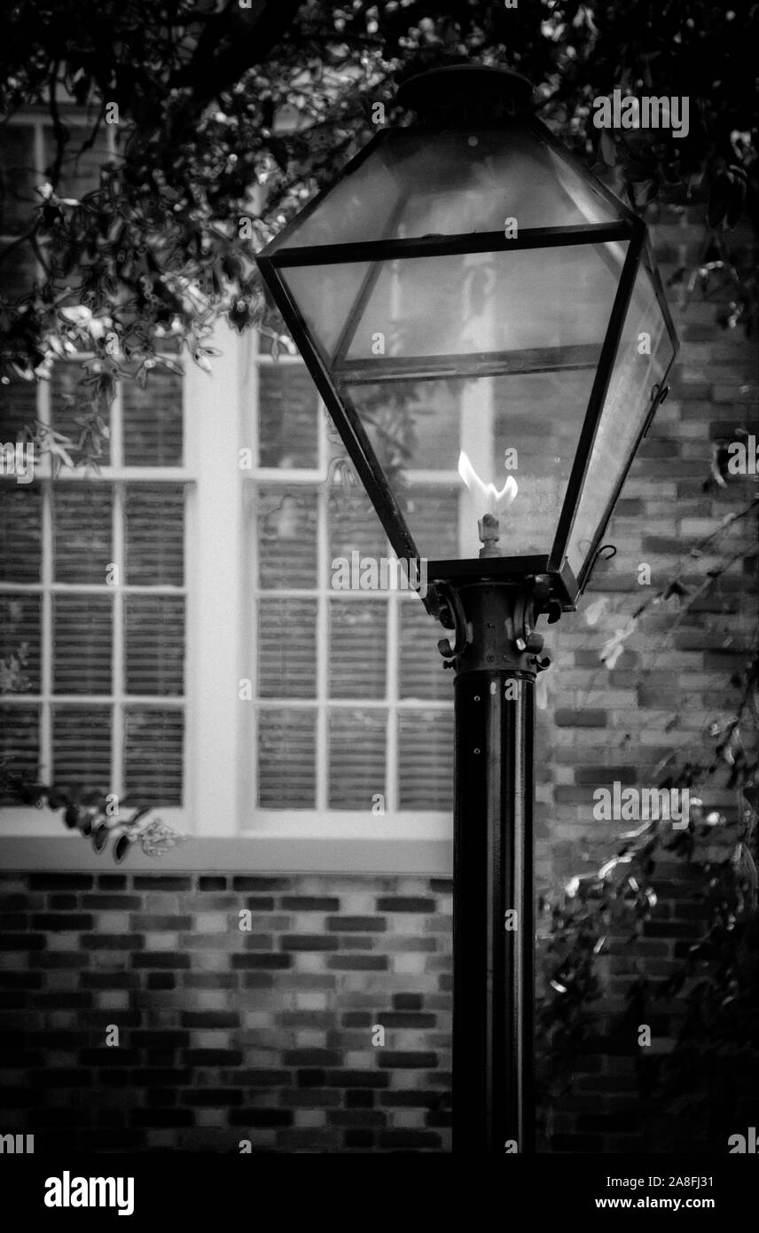 A single antique style gas lamp post alight, near white framed windows ...