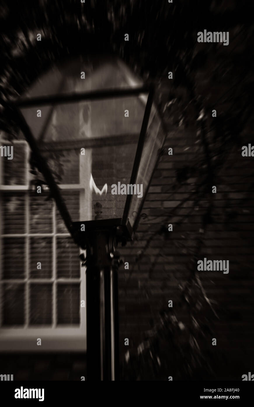 A single antique style gas lamp post alight, near white framed windows ...