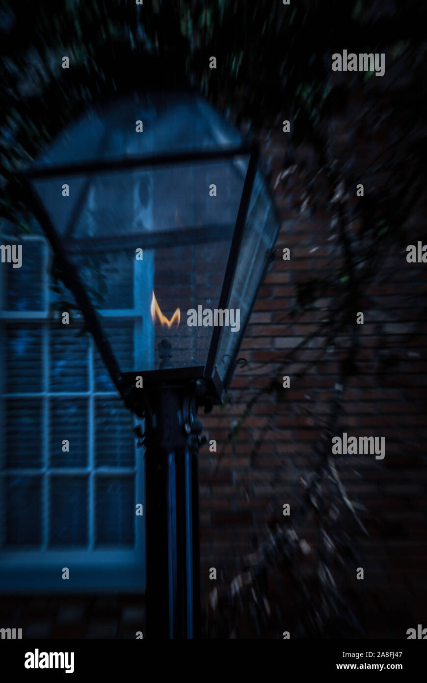 A single antique style gas lamp post alight, near white framed windows ...