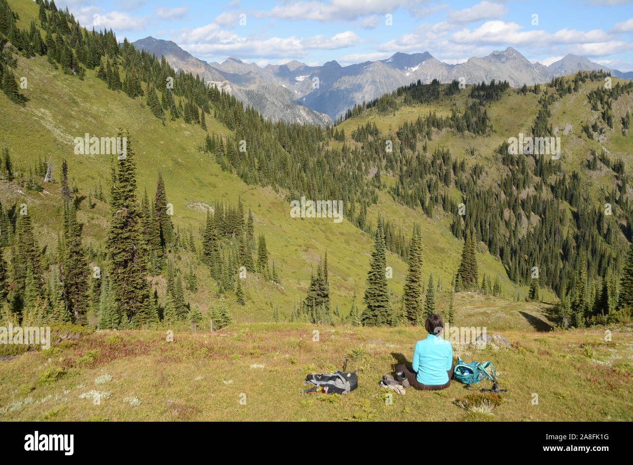 A female hiker on a sub-alpine ridge facing the mountains of Goat Range ...