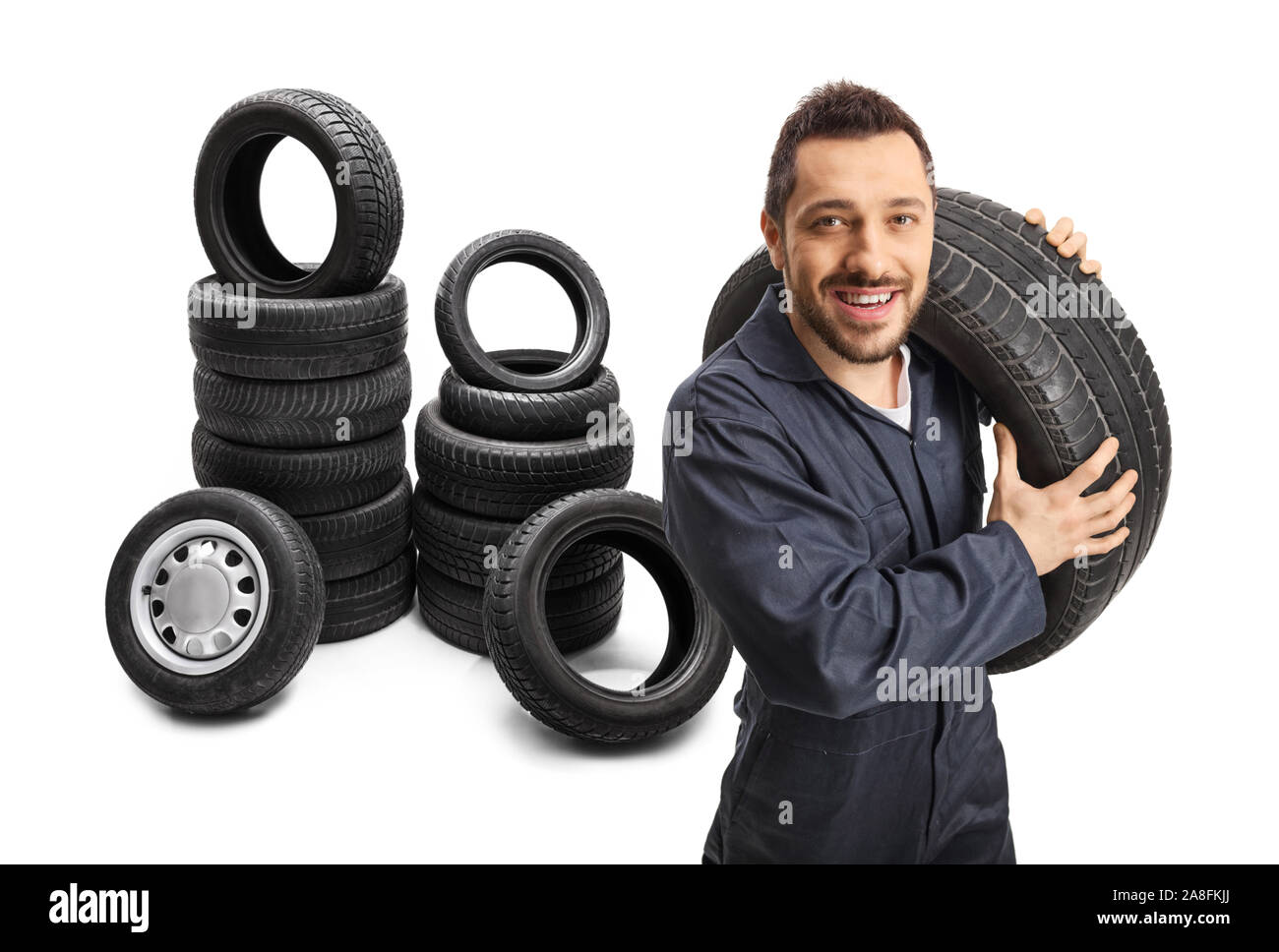 Mechanic carrying a vehicle tire with piles of tires behind him ...