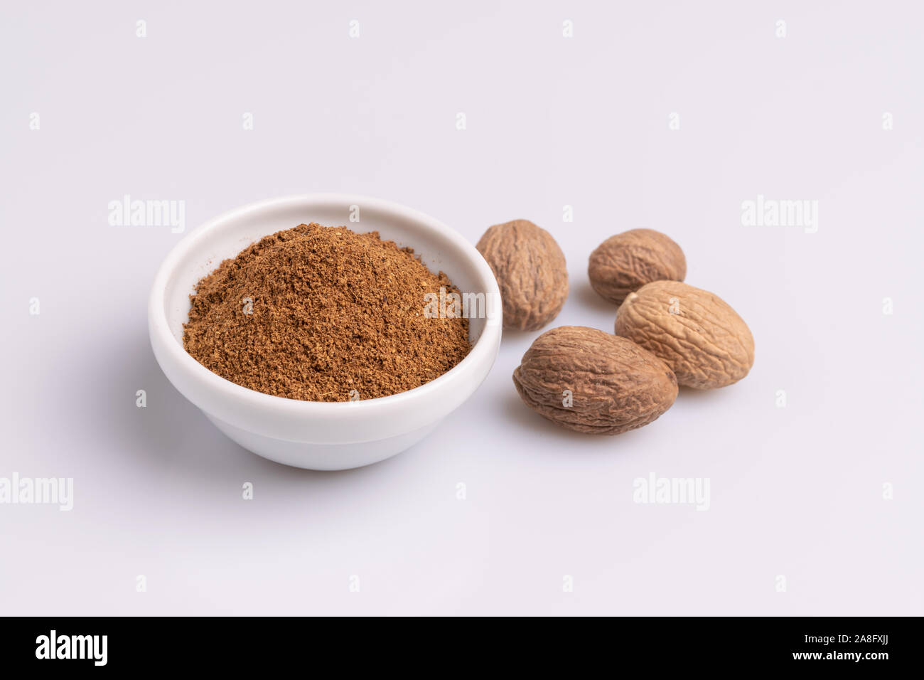 Ground nutmeg spice in white ceramic bowl isolated on white background ...