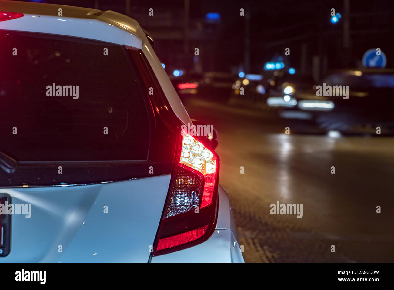 A tail-light of car at night city. A red light at the rear of a white ...