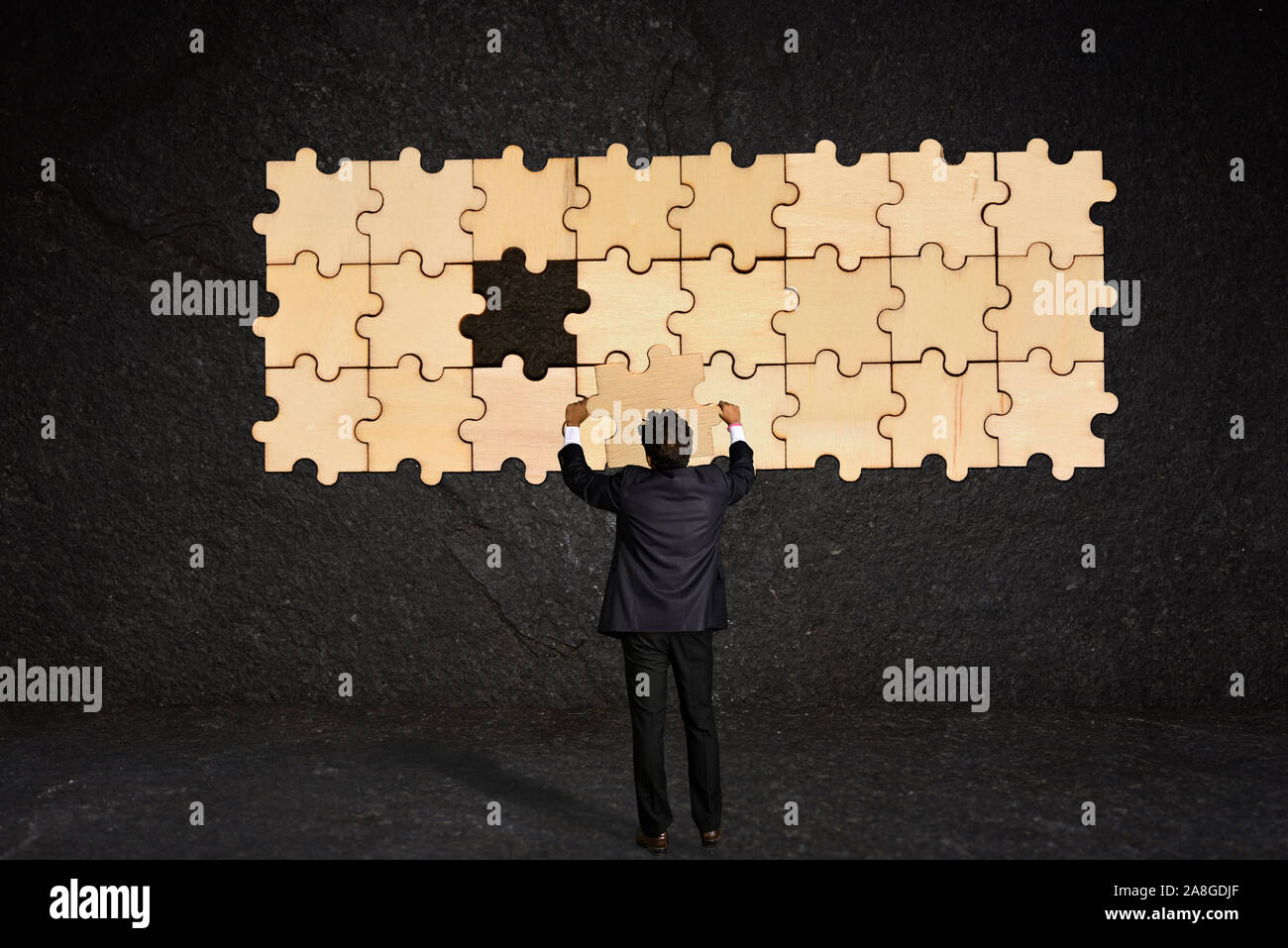 A businessman holding the missing piece of puzzle to an unfinished ...
