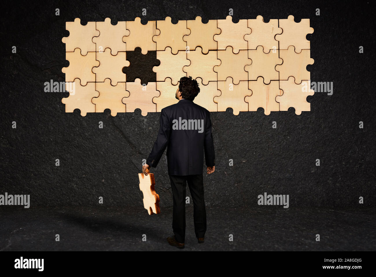 A businessman holding the missing piece of puzzle to an unfinished ...