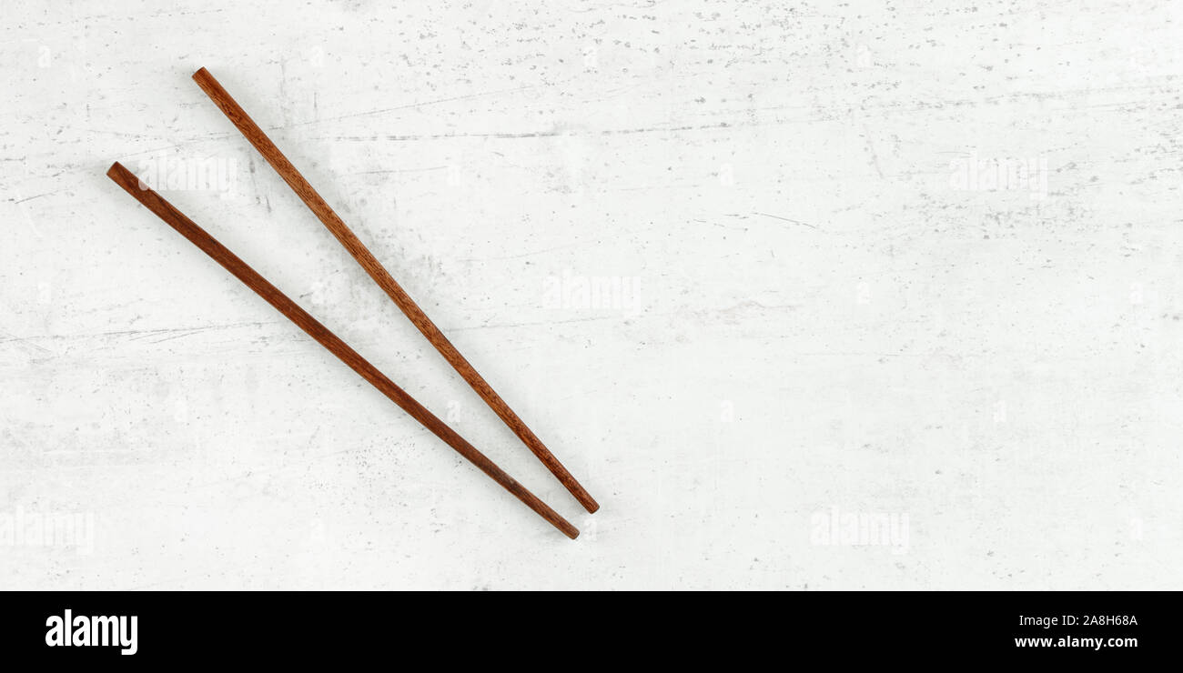 Flat lay photo - pair of dark wood chopsticks on white board. Wide ...