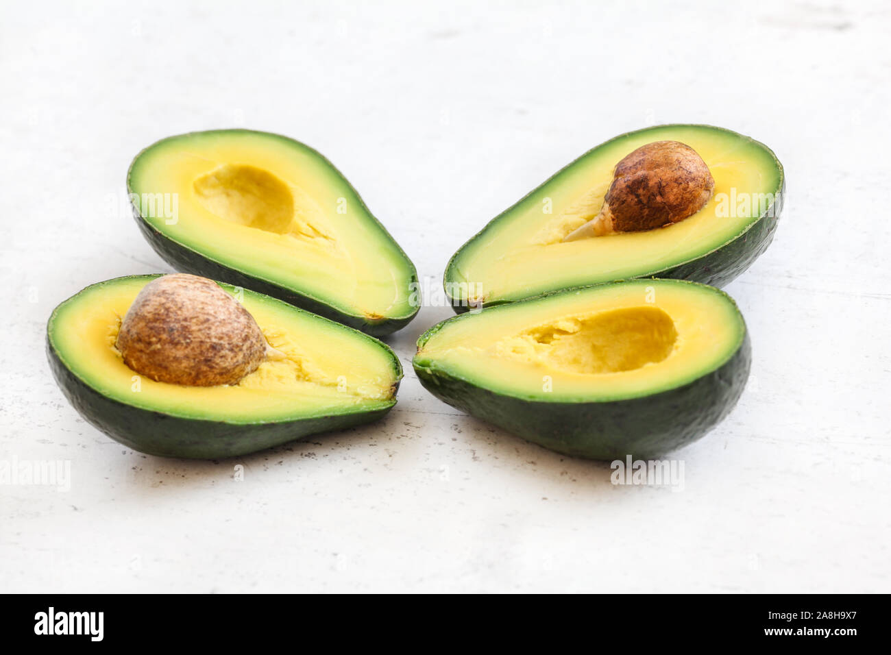 Two avocados cut in half, seed showing, on white working board Stock ...