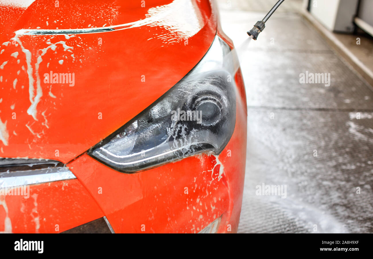 Front light of red car washed in self serve carwash, jet water spraying ...