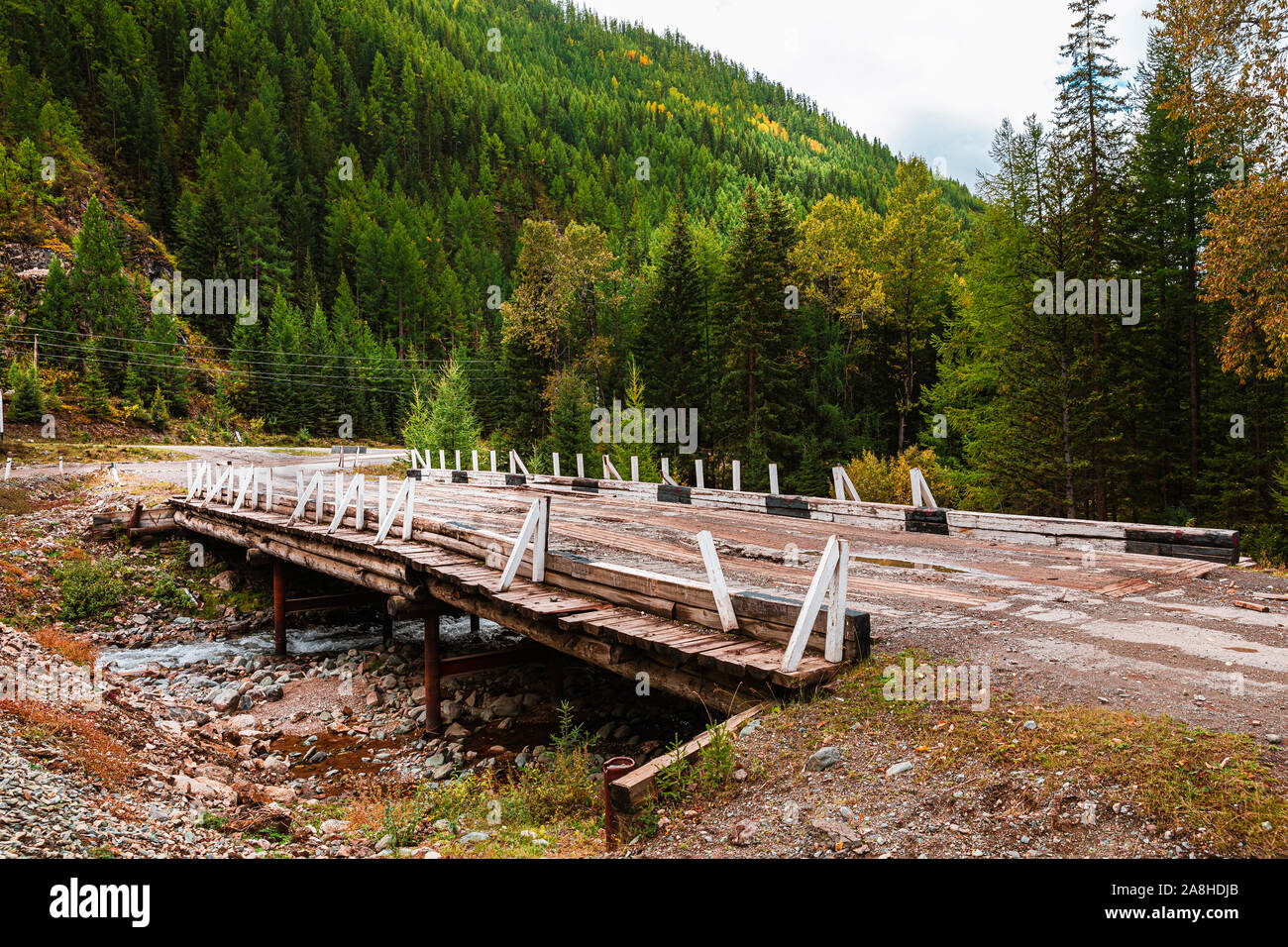 Old ruined wooden bridge over the river in the forest in cloudy weather ...