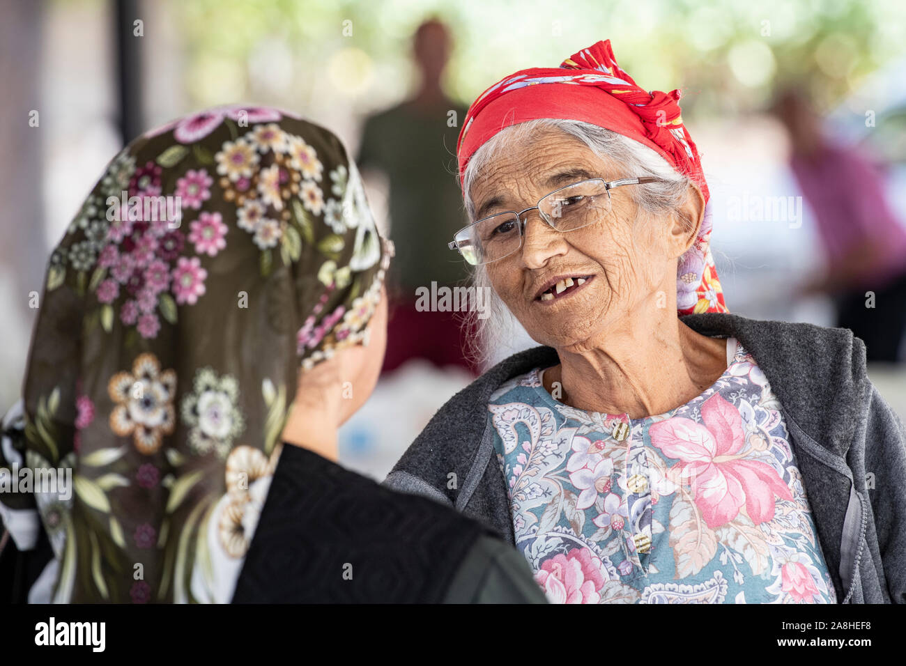 A lady with missing teeth and a red head scarf talks to her friend in a ...