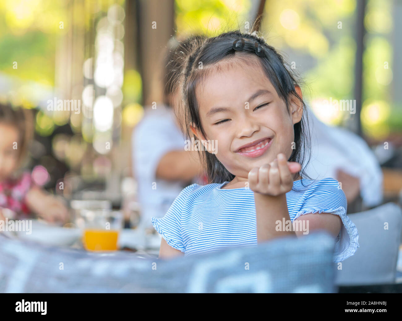 Cute child girl with big smile at table in a resort, trying to make ...