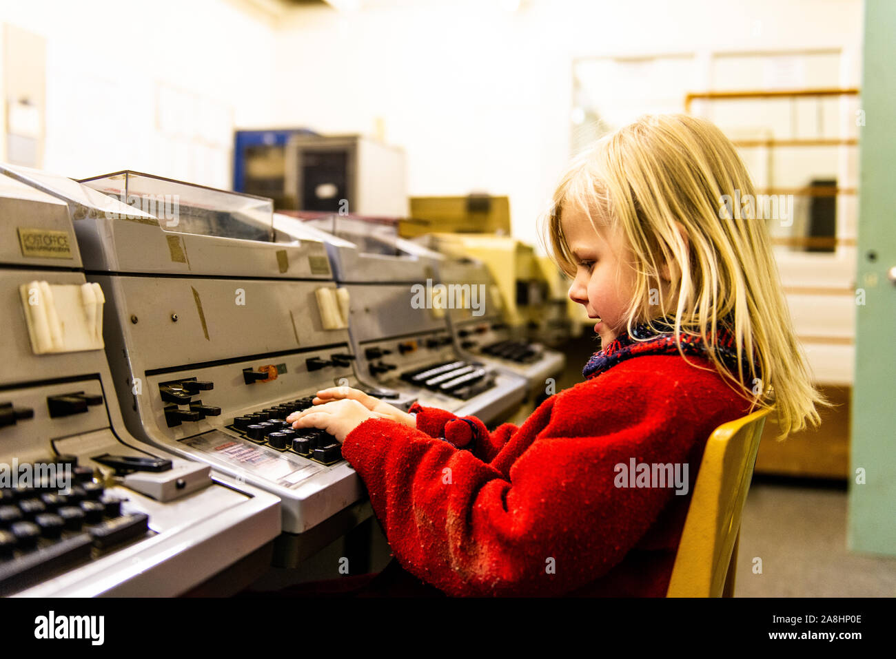 A cute little girl in a red coat sits at an old fashioned computer ...