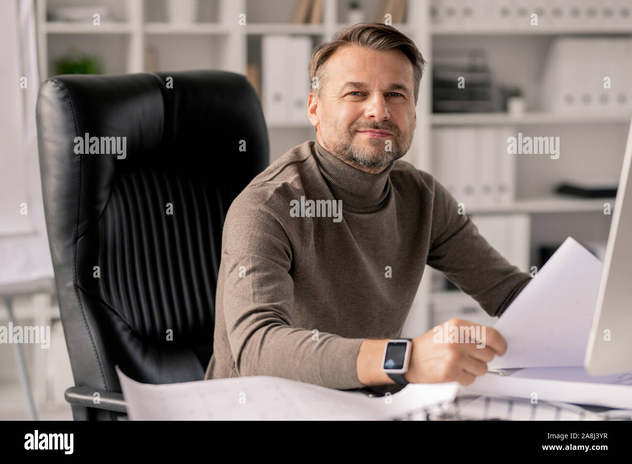 Successful mature engineer with papers looking at you while in armchair ...