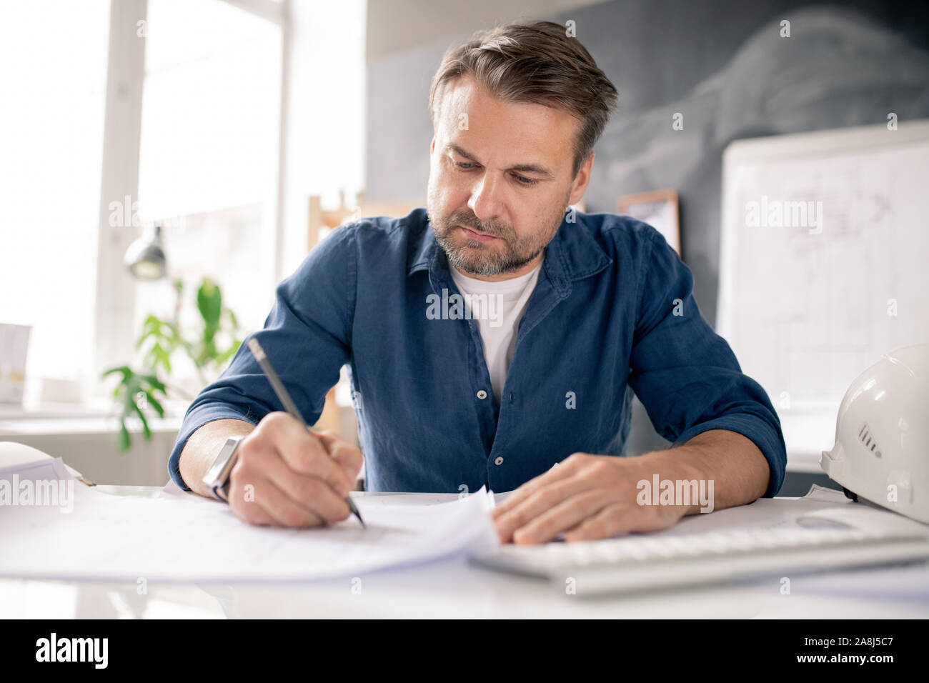 Serious architect with pencil drawing new sketch on paper while bending ...