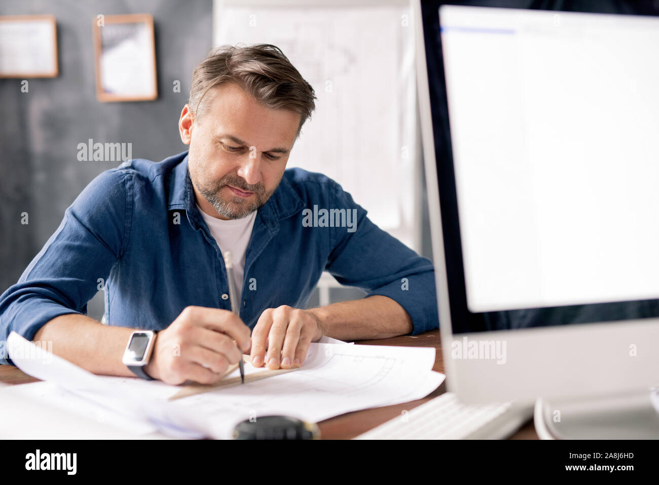 Professional engineer with pencil pointing at blueprint while drawing ...