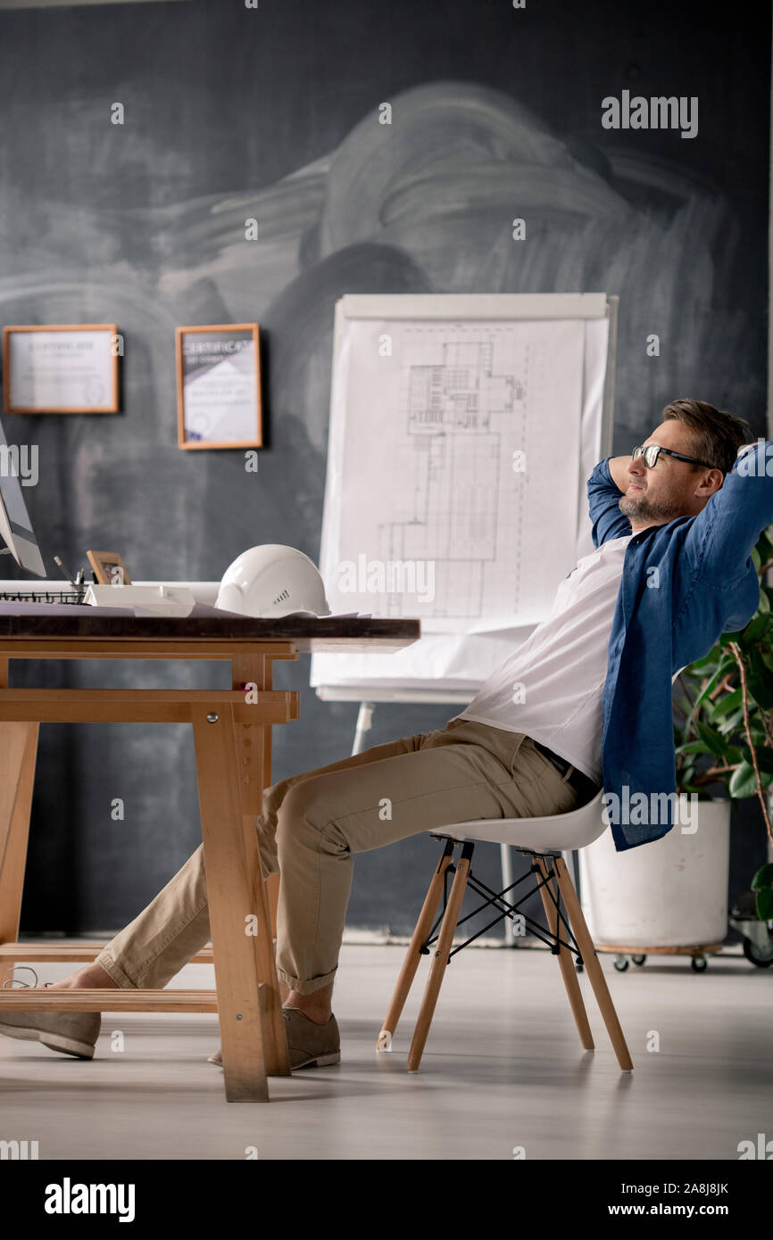Relaxed engineer sitting on chair by table and watching video on ...