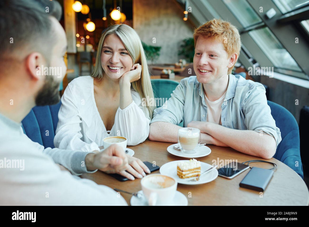 Happy young casual couple chatting to their friend by cup of coffee and ...
