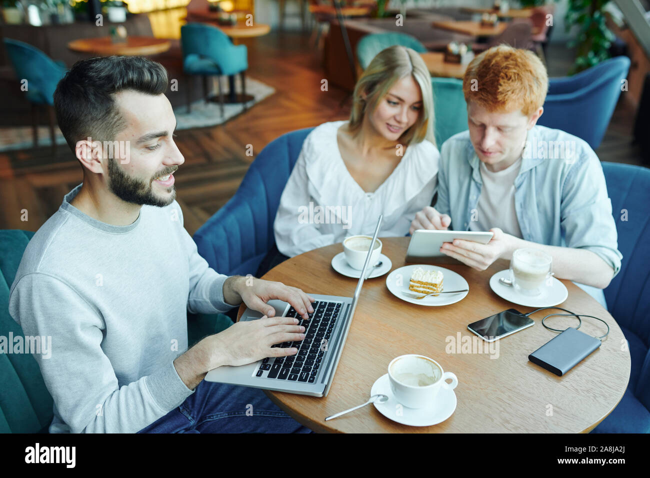 Young casual man networking in front of laptop while his friends using ...