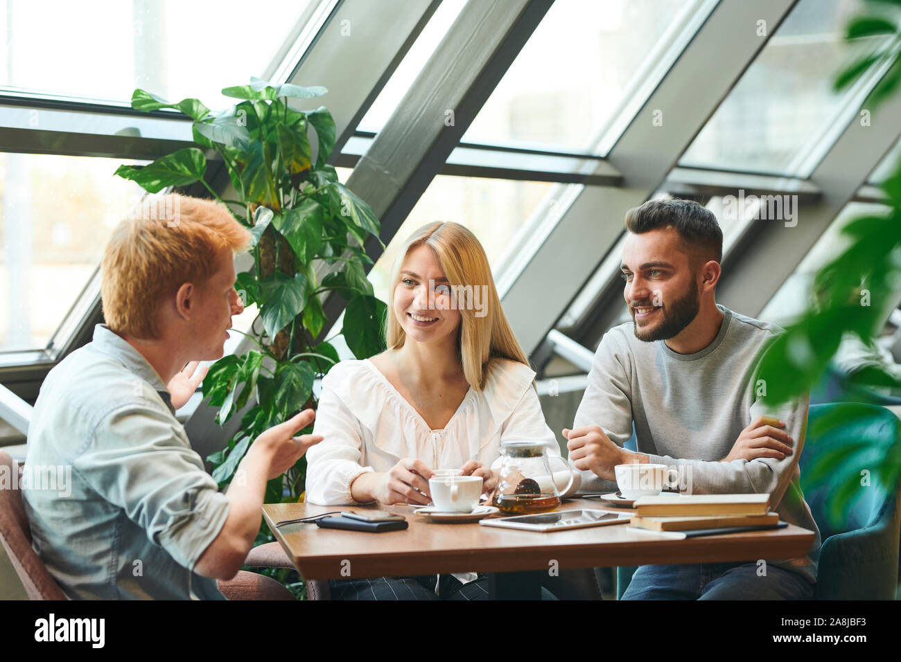 Group of young contemporary students gathered by table in cafe after ...