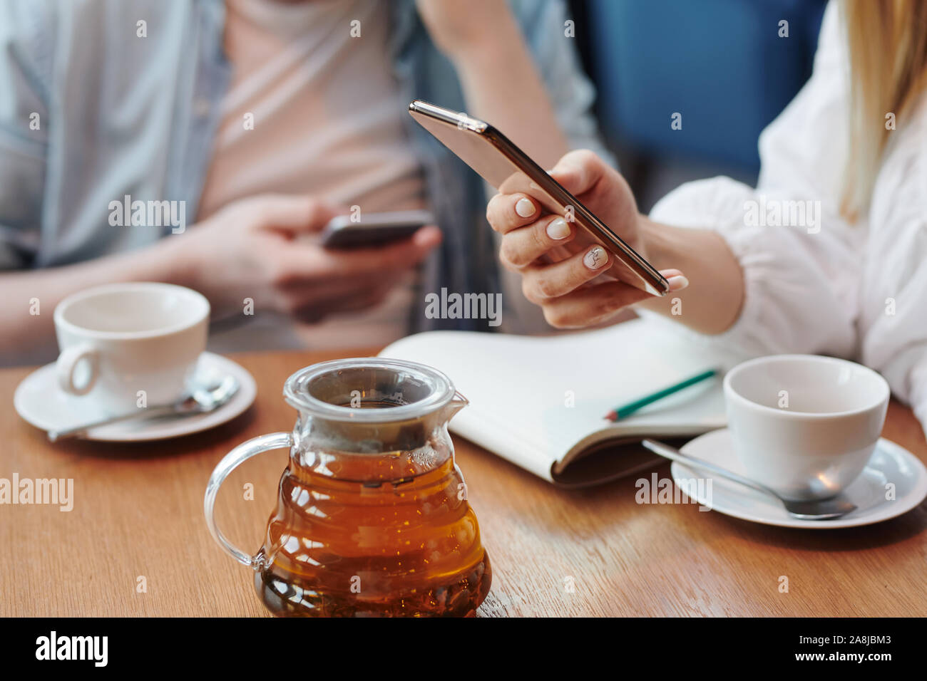 Hand of female millennial scrolling in smartphone over table while ...