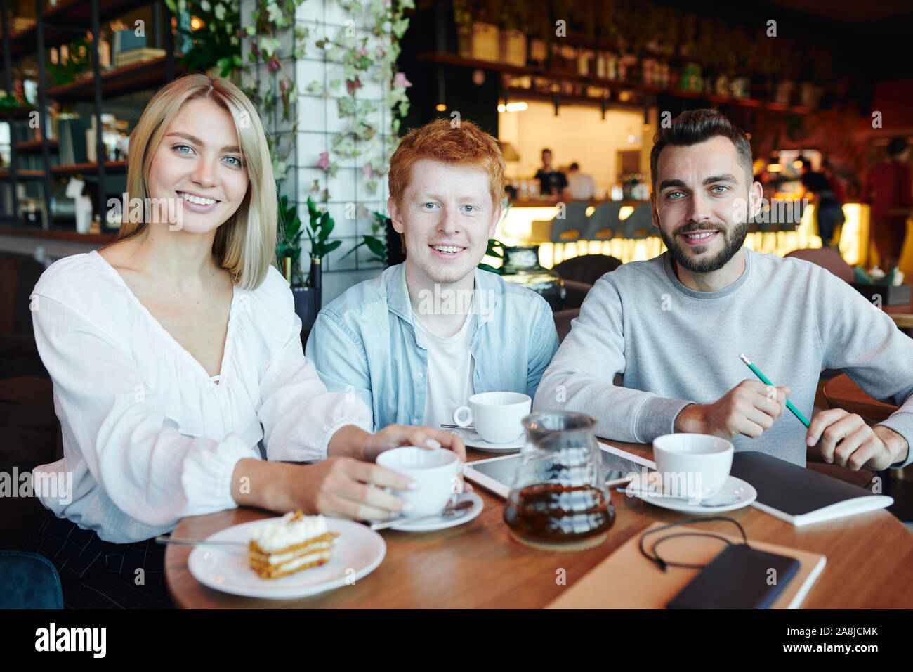 Restful happy students of college sitting by table in cafe after ...