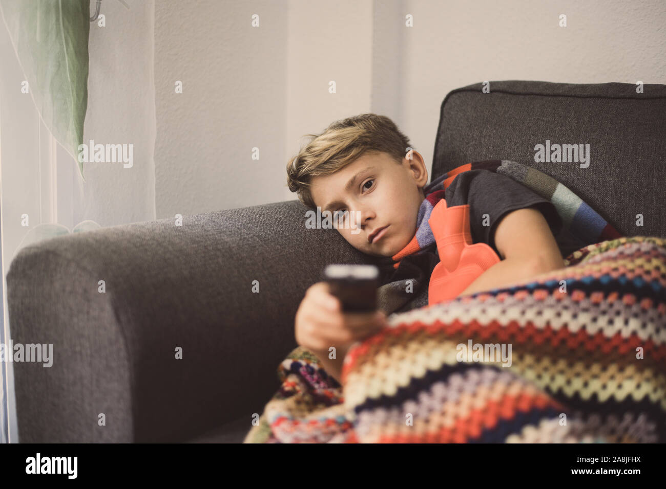 Sick boy watching tv with woolen blanket and hot water bottle. Sad teen ...