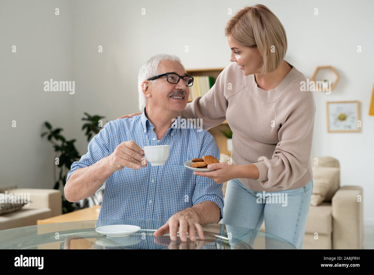 Careful daughter bringing cookies to her happy retired father with cup ...