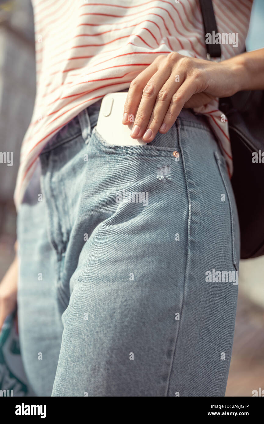Young slim girl putting smartphone into pocket Stock Photo - Alamy