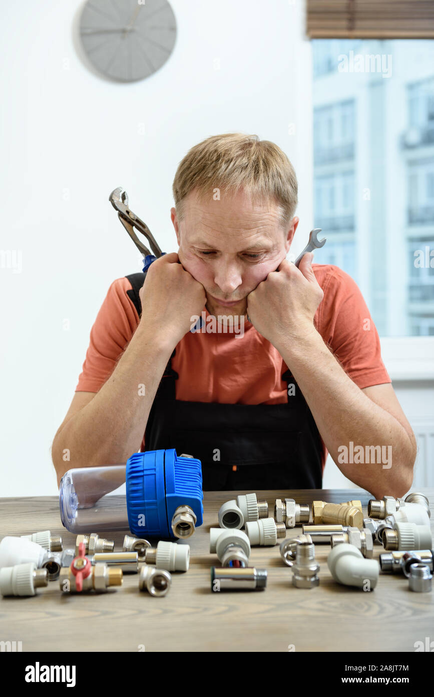The worker is thinking and looking at the elements of the plumbing. He ...