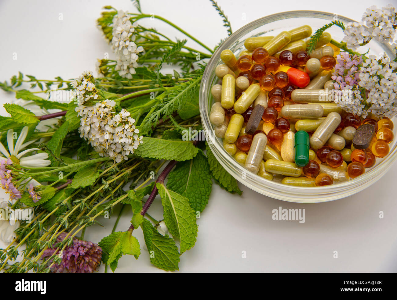 A bowl with various capsules and tablets, medicinal and aromatic herbs ...