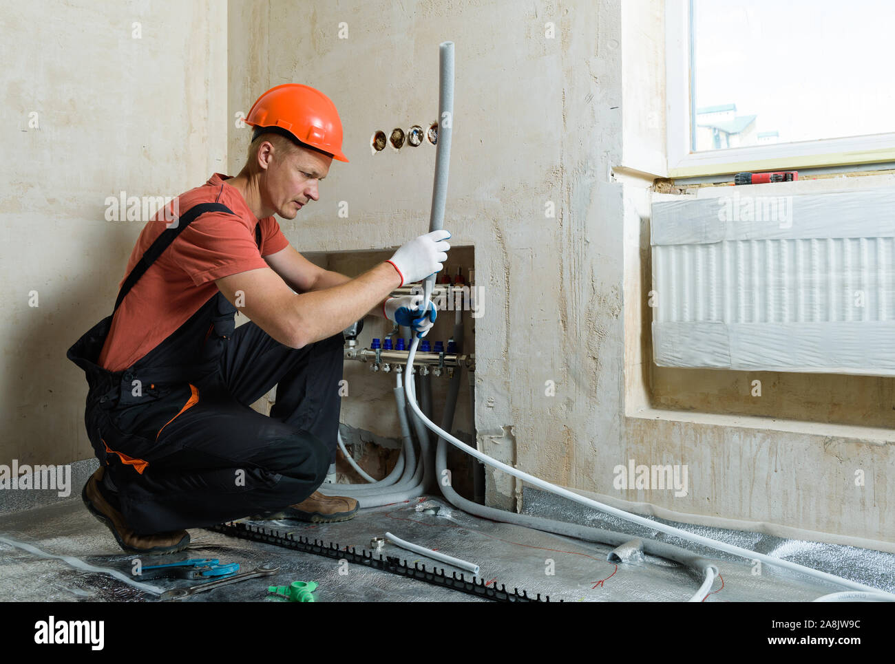 The worker is installing a pipe for the warm floor in the apartment. He ...