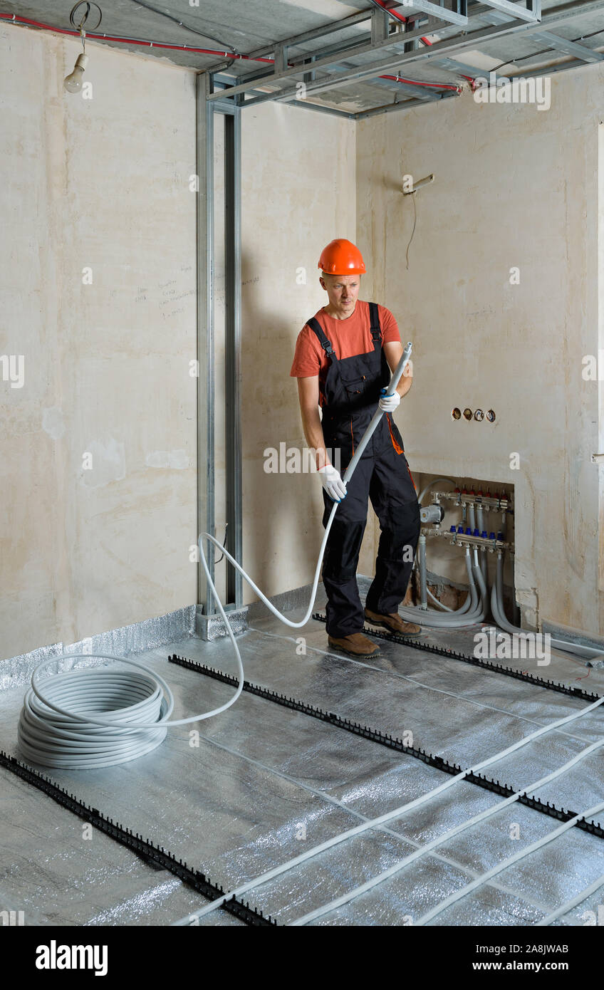 The worker is installing a pipe for the warm floor in the apartment. He ...