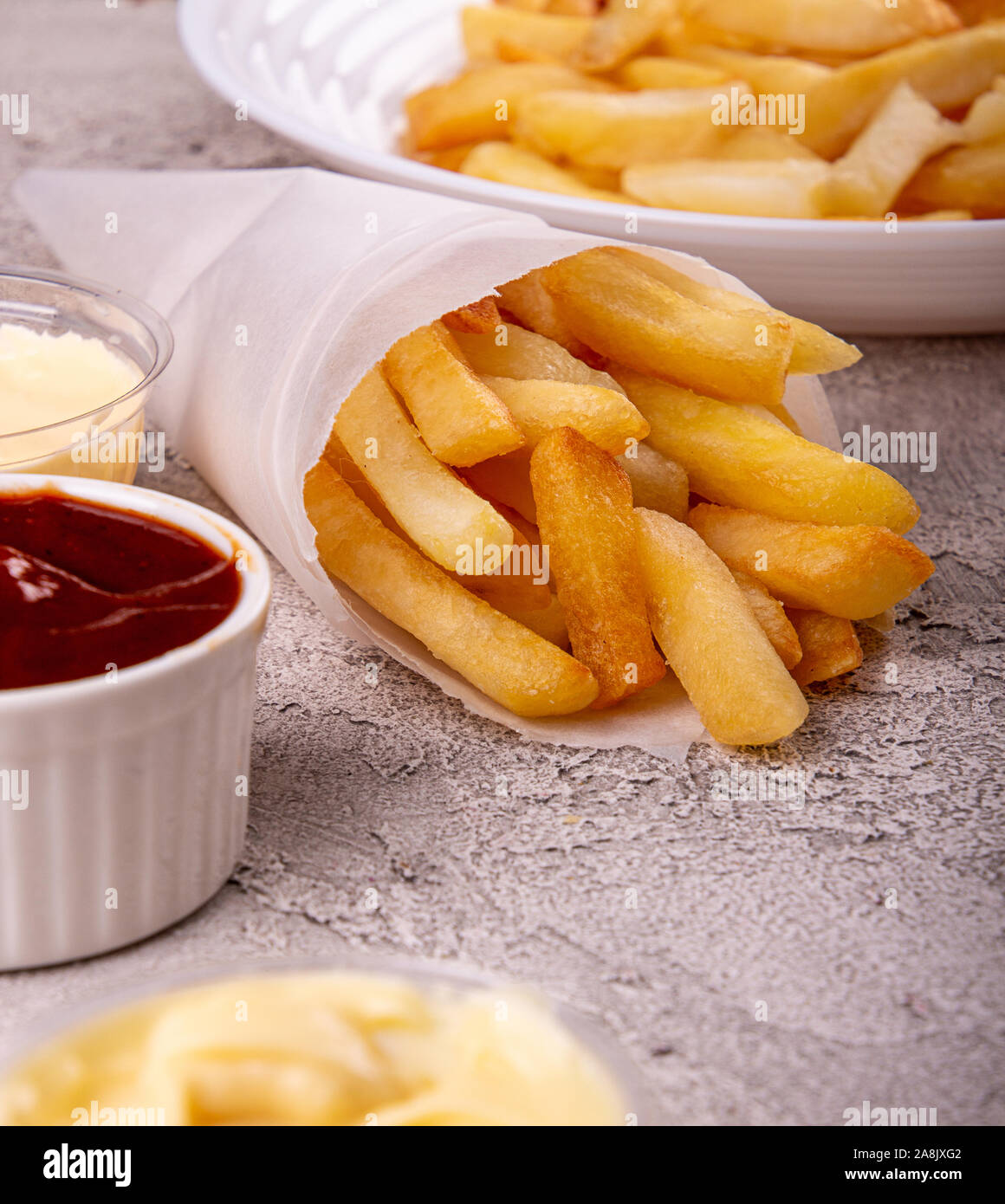 paper conus of french fries chips potato and sauces on gry concrete ...