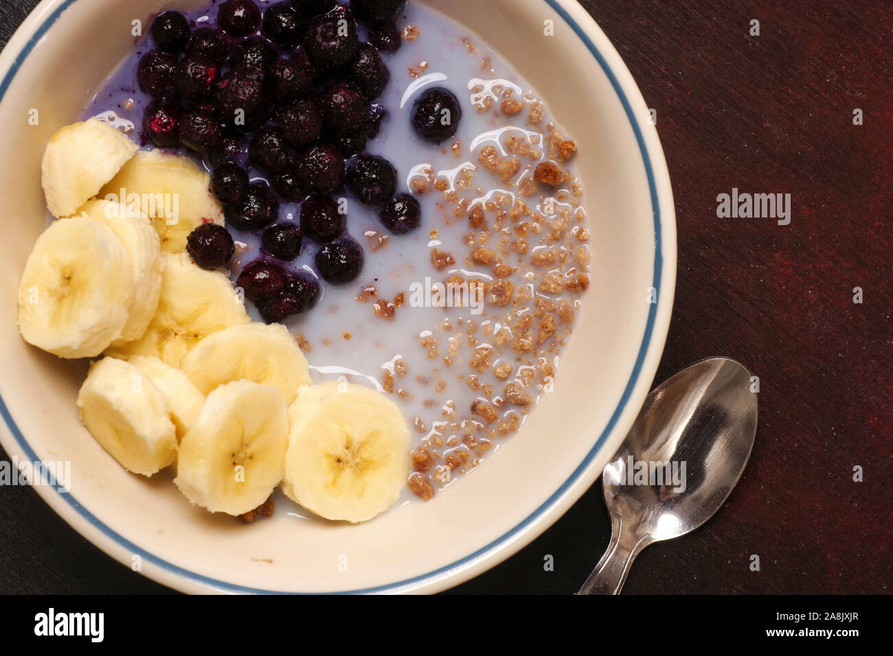 Cold cereal breakfast with milk,blueberries,and bananas against dark ...