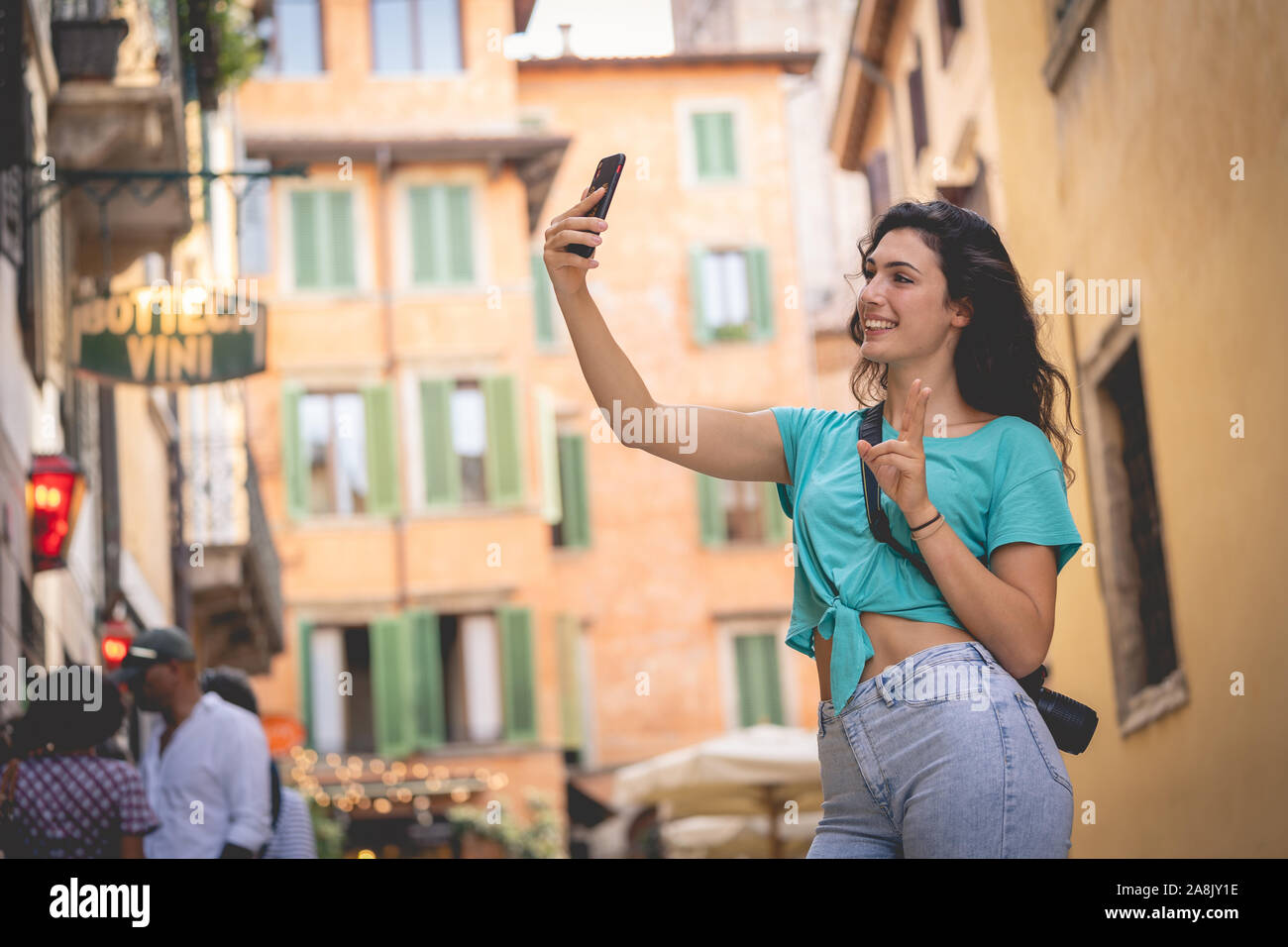 Tourist girl on vacation in Verona taking a selfie on a typical street ...