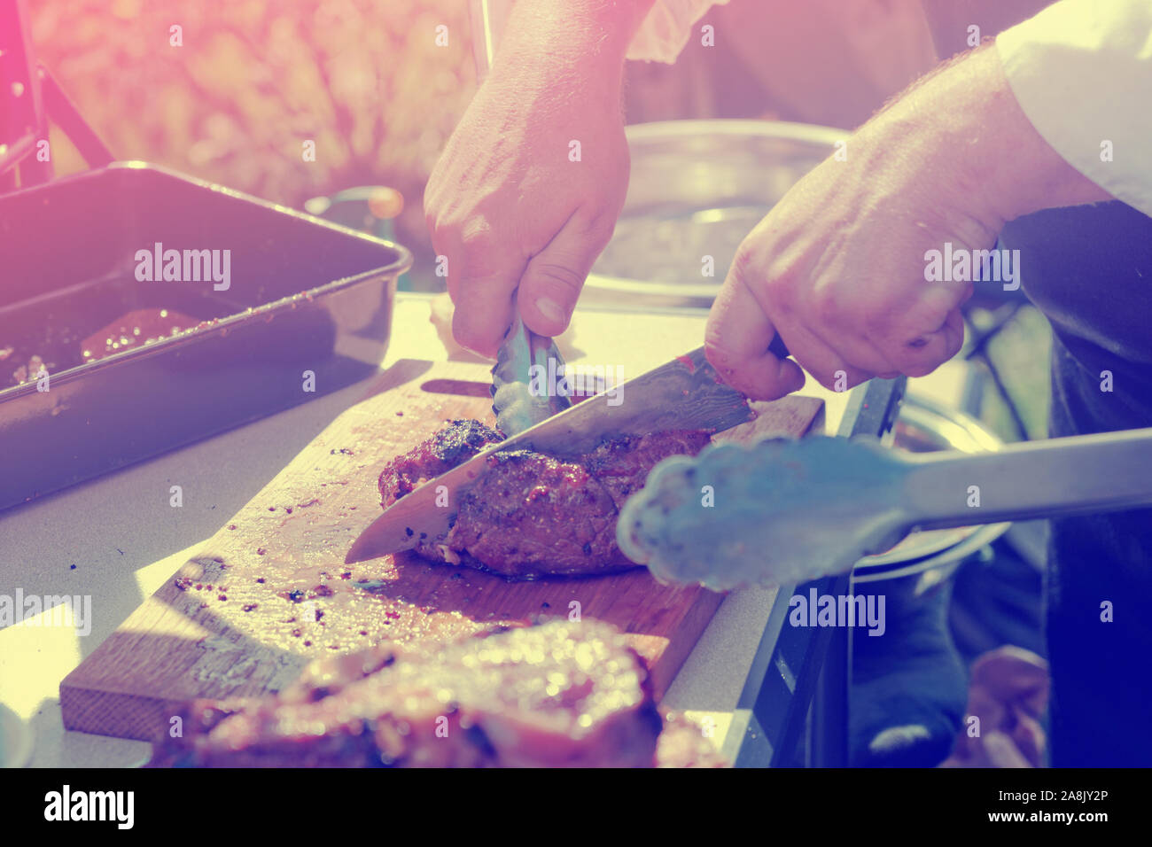 Chef is cutting meat at outdoor kitchen, toned image Stock Photo - Alamy