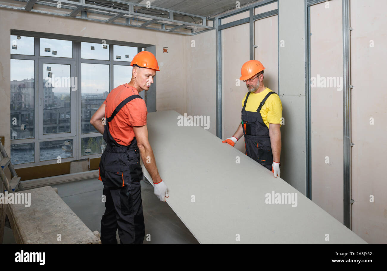 Workers are carrying plasterboard for further attachment to the wall ...