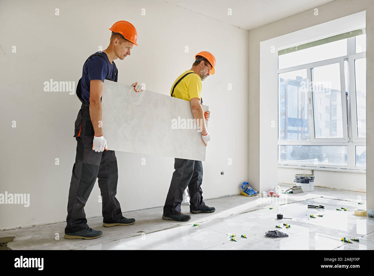 Workers are carrying a large ceramic tile for installation on the floor ...