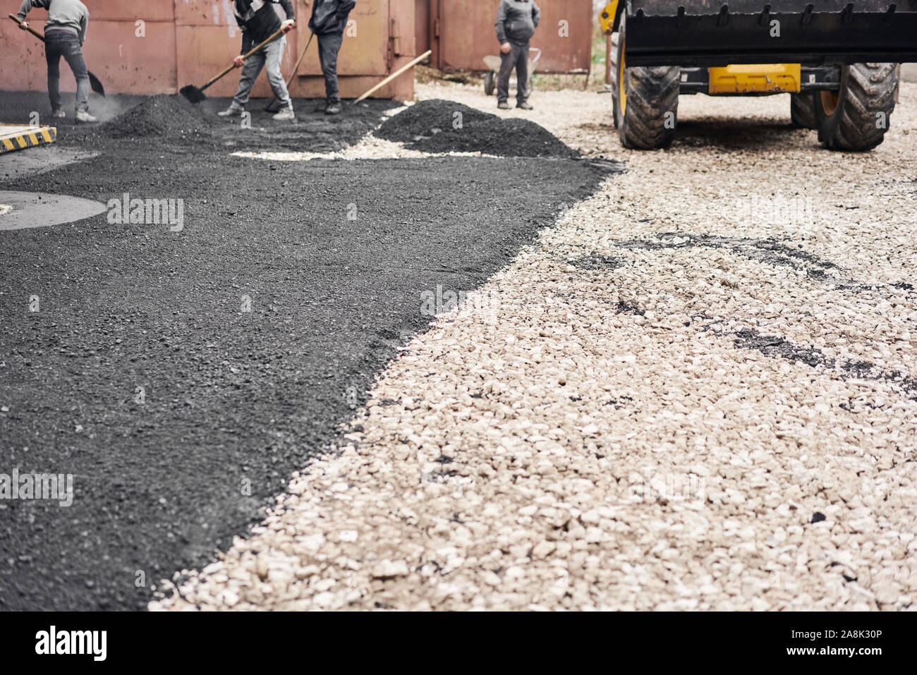 Laying new asphalt, covering the pit, on the rubble. Workers carry in ...