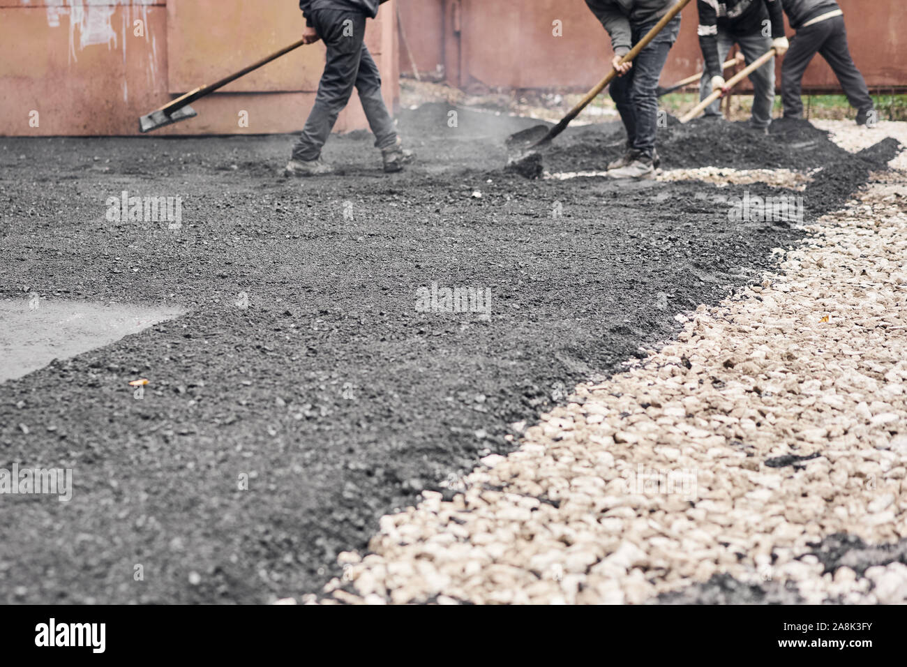 Laying new asphalt, covering the pit, on the rubble. Workers carry in ...