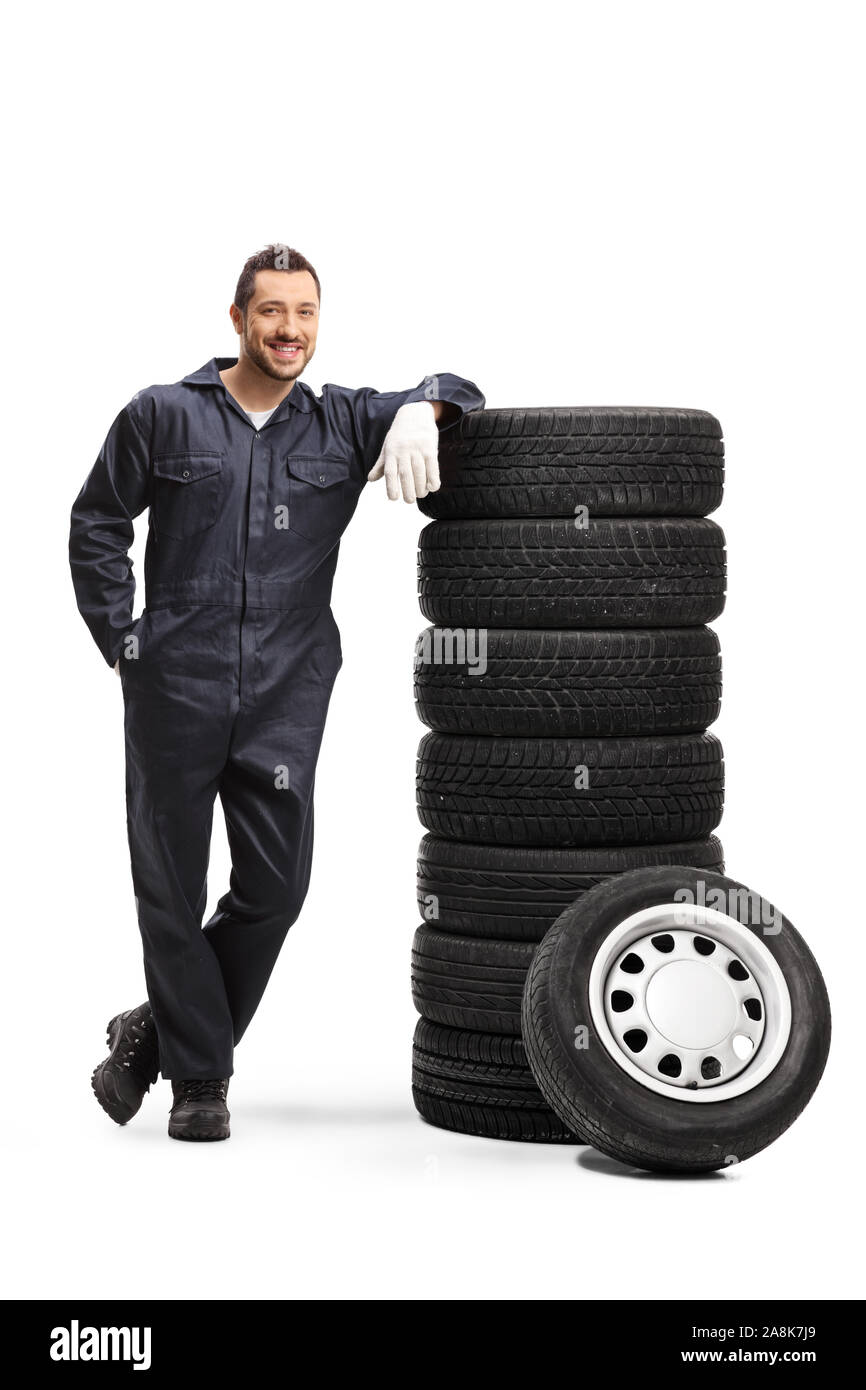 Full length portrait of a car repair worker posing with a pile of tires ...