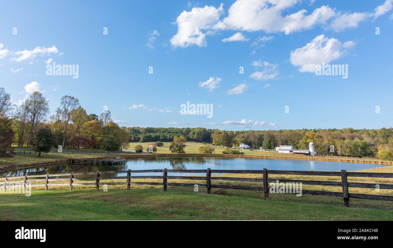 Fence by a pond with a farm with a barn and silo in the background in ...