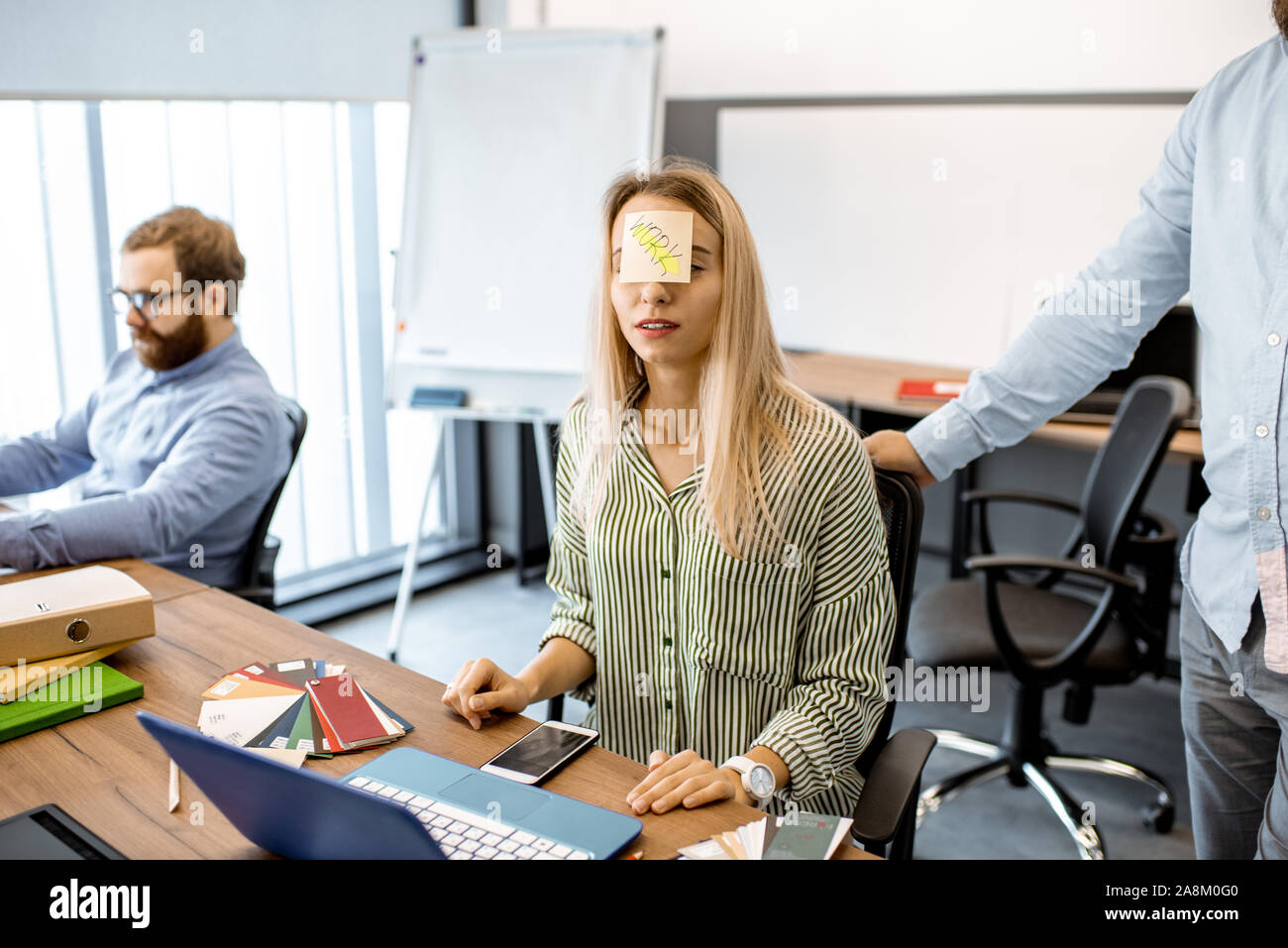 Young woman with work reminder sticker on her head feeling tired during ...