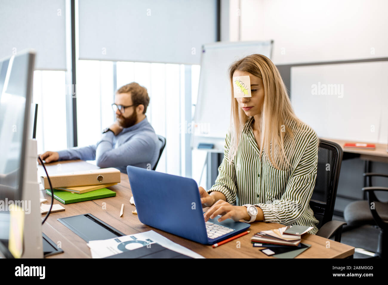 Young woman with work reminder sticker on her head feeling tired during ...