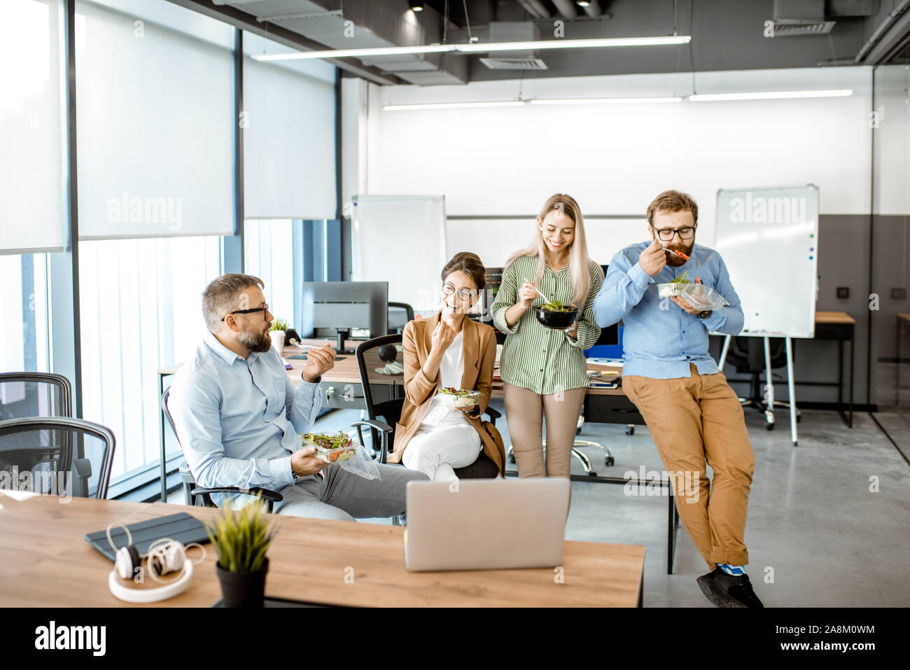 Group of diverse colleagues eating takeaway salad, sitting together and ...