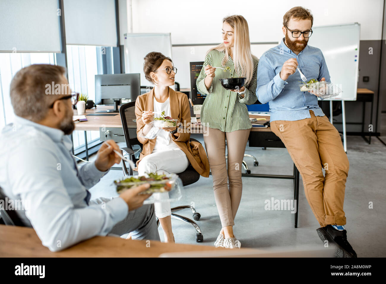 Group of diverse colleagues eating takeaway salad, sitting together and ...