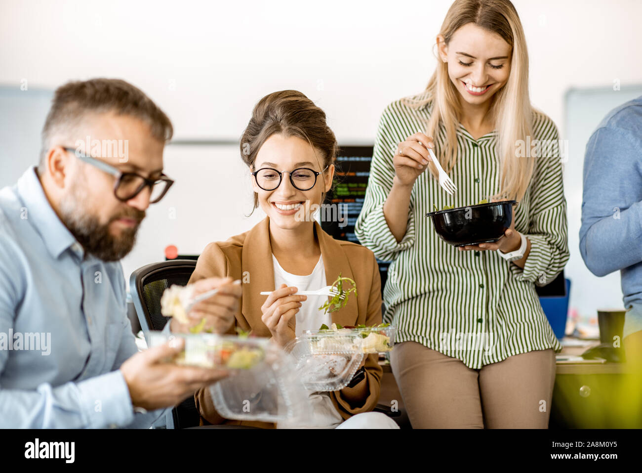 Group of diverse colleagues eating takeaway salad, sitting together and ...