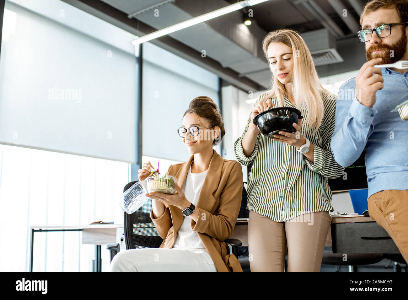 Group of diverse colleagues eating takeaway salad, sitting together and ...