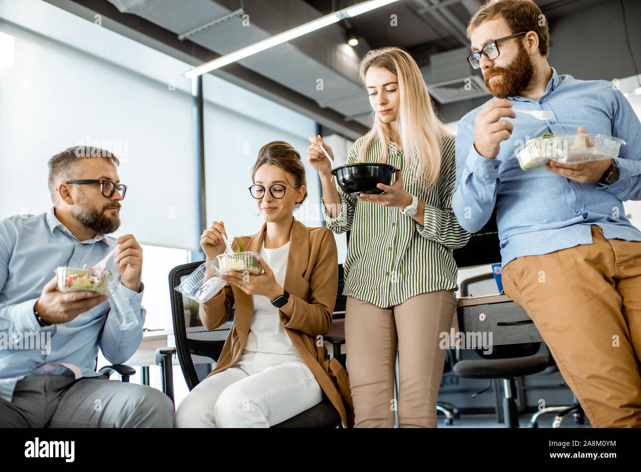 Group of diverse colleagues eating takeaway salad, sitting together and ...