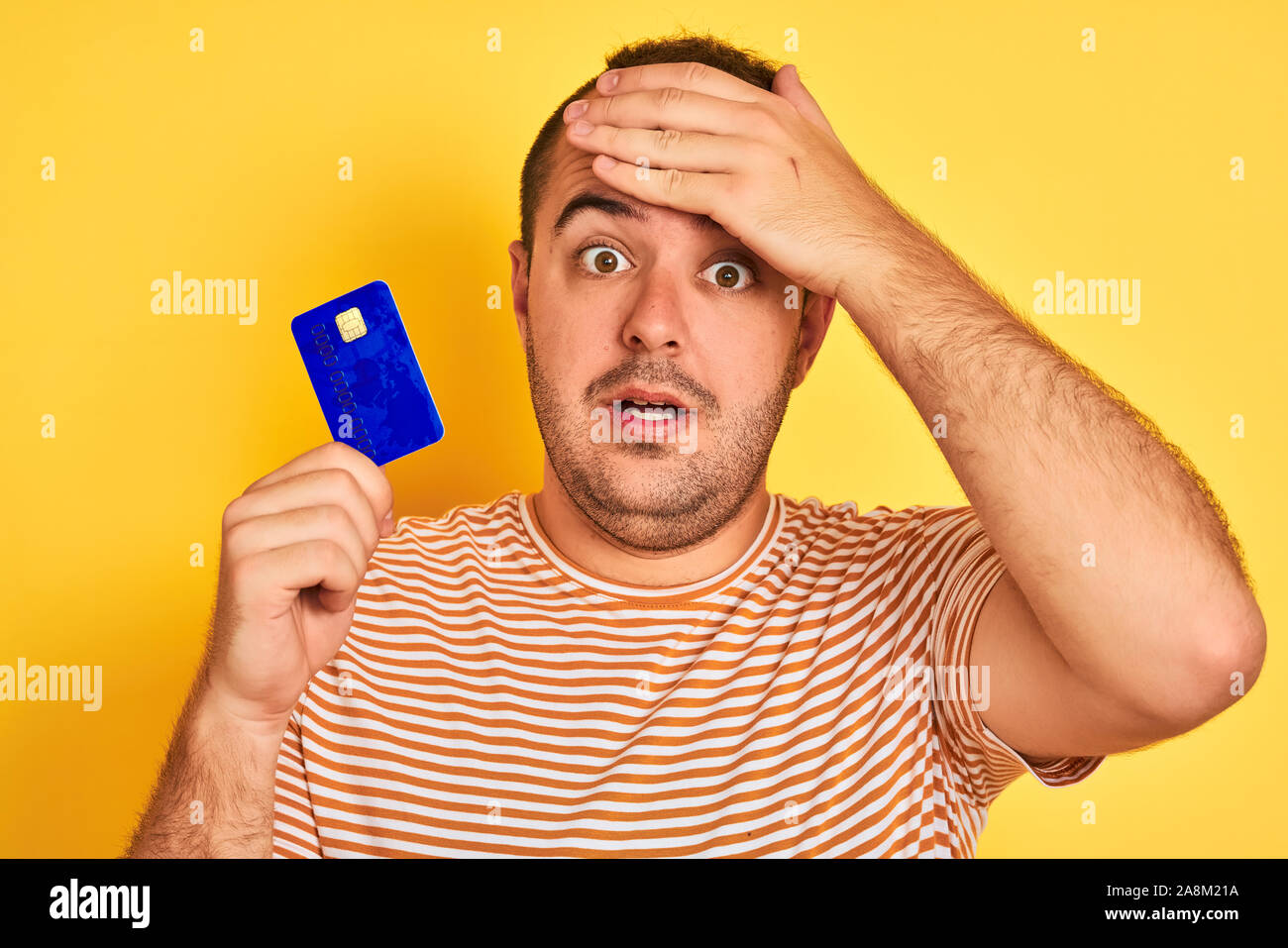 Young man holding blue credit card standing over isolated yellow ...